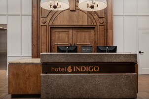 Uma receção com um painel de madeira ao fundo, dois balcões pretos e um letreiro com a inscrição "hotel INDIGO".