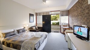 Quarto de hotel com cama, televisão, escrivaninha e vista para o exterior.
