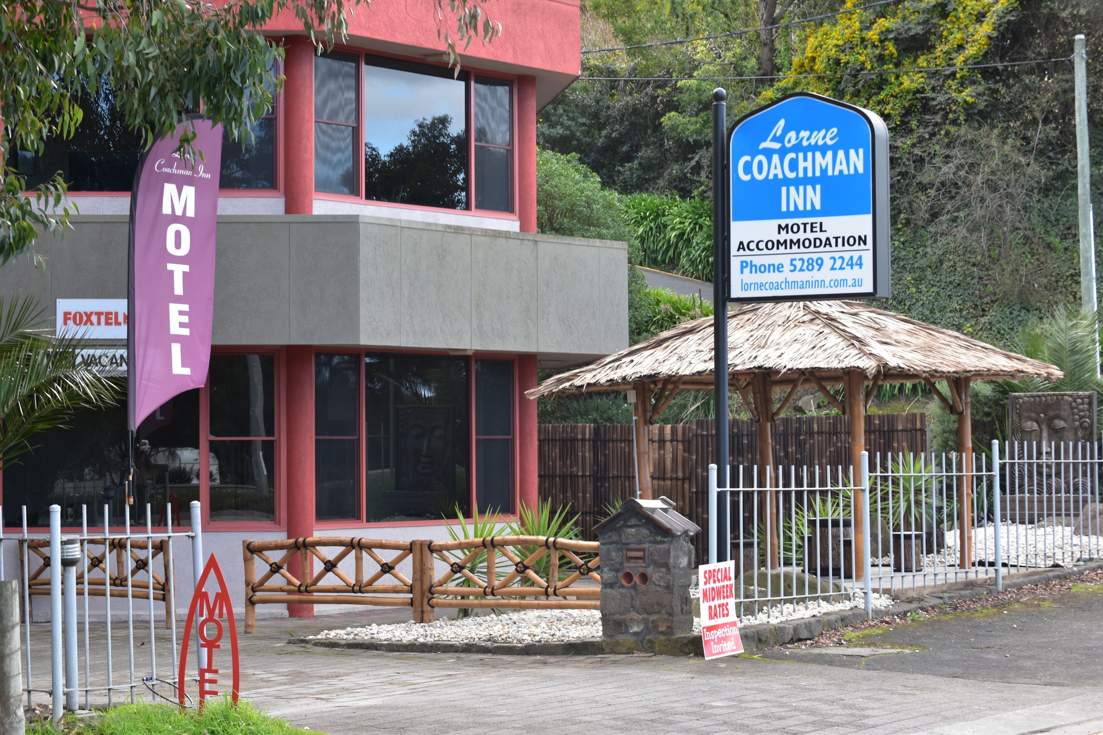 Um motel com um edifício vermelho e cinza, uma cerca de madeira e uma placa com o nome Coachman Inn.