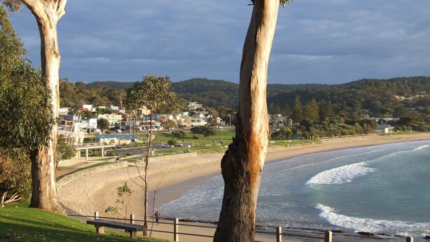 Vista costeira com praia, um caminho para passear e uma cidade ao fundo.