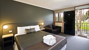 Quarto de hotel com cama, mesas de cabeceira, uma cadeira e porta de correr para uma varanda.