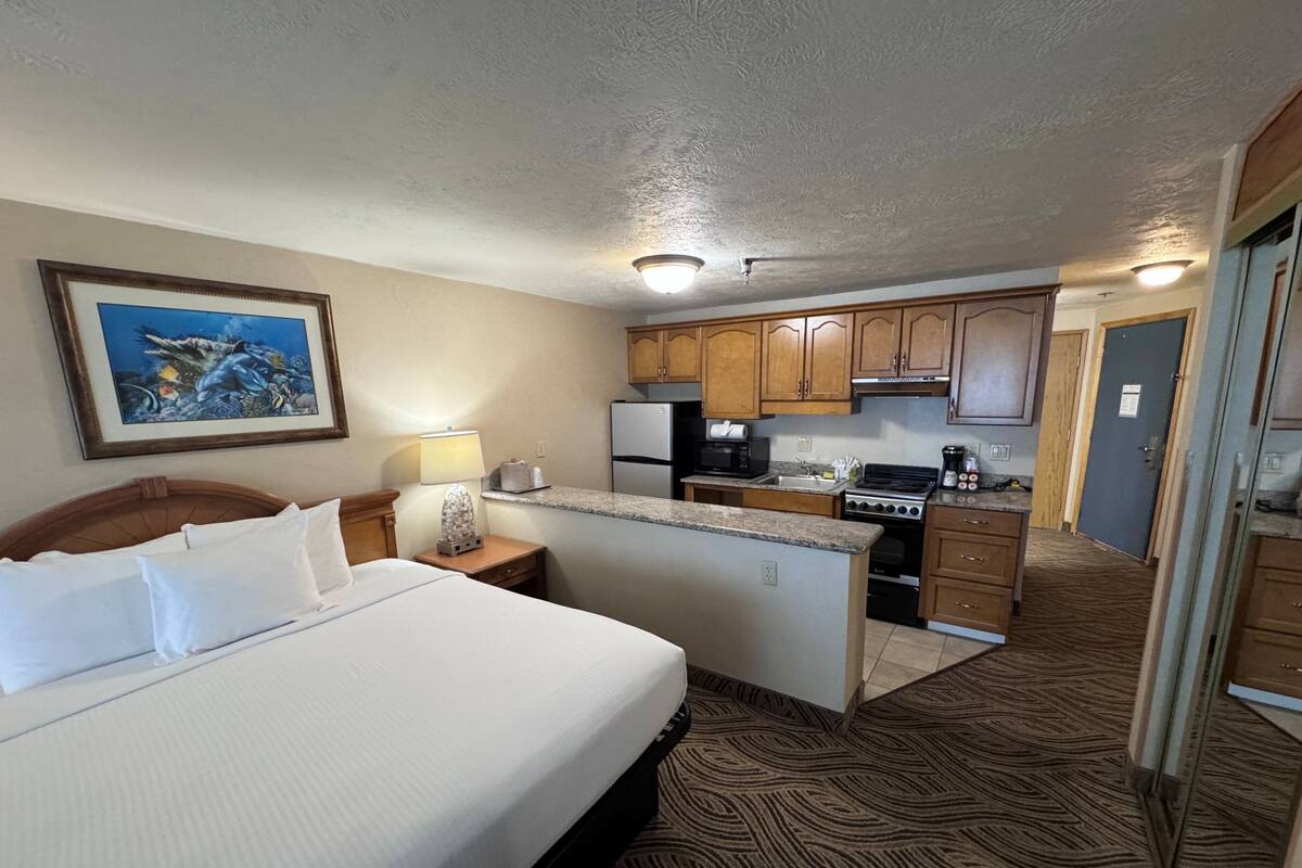 Quarto de hotel com cama, pequeno espaço de cozinha e banheiro.
