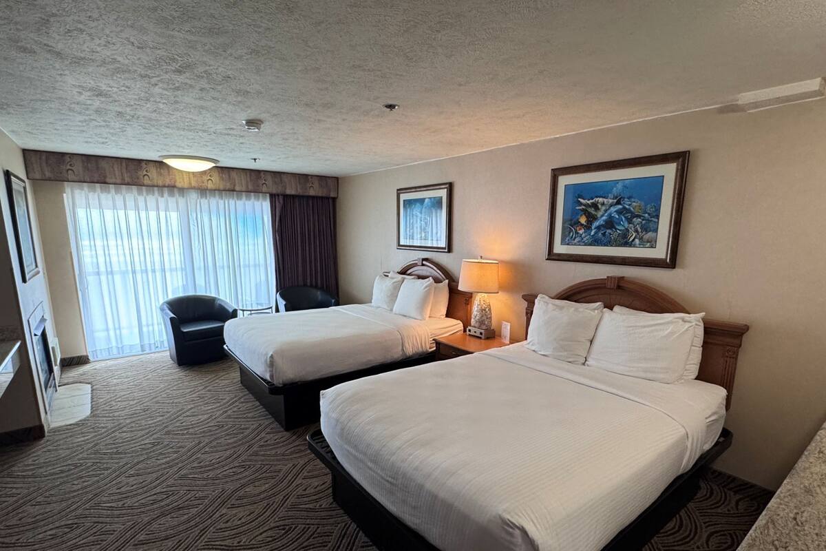 Quarto de hotel com duas camas, uma escrivaninha, uma cadeira, um abajur e um quadro na parede.