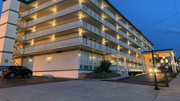 Um hotel com vários andares, varandas, área de estacionamento e entrada bem iluminada.