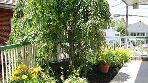 Varanda com guarda-corpo branco, uma árvore e plantas em vasos com flores amarelas.