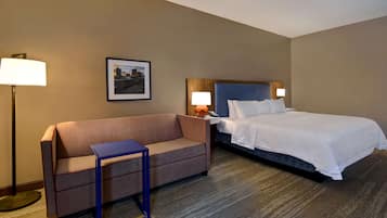 Quarto de hotel com cama, sofá, mesinha e um quadro na parede.