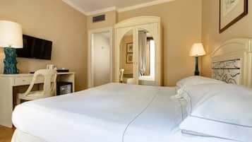 Quarto de hotel com cama, escrivaninha com cadeira, televisão, espelho e abajur.