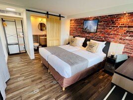 Quarto de hotel moderno com uma cama grande, parede de tijolos e uma fotografia de paisagem urbana.