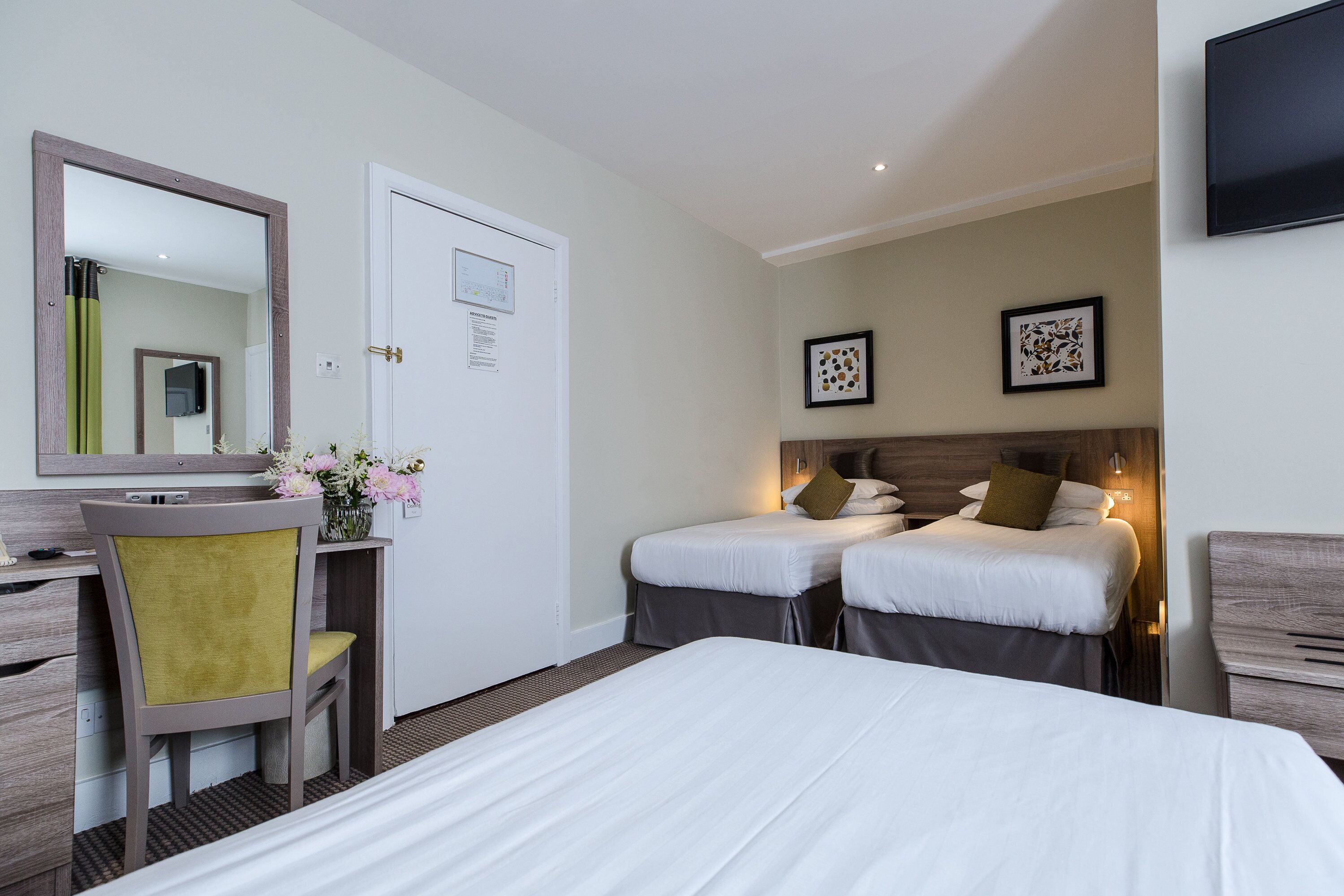 Quarto de hotel com duas camas, uma escrivaninha, uma cadeira, um espelho e uma televisão.