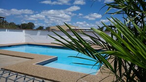 Piscina com água azul cristalina, cercada por um muro branco e um deck de concreto.