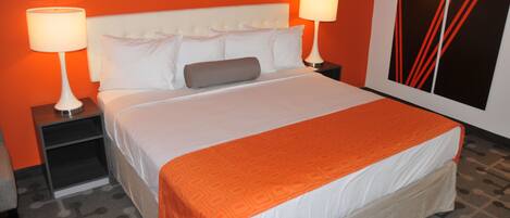 Quarto de hotel com uma cama grande, duas mesas de cabeceira com luminárias, uma parede de destaque vermelha e um tapete com padrão geométrico.