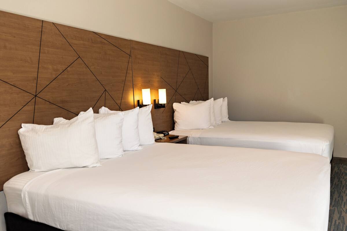 Quarto de hotel com duas camas, uma cabeceira de madeira, luminárias de cabeceira e um telefone.