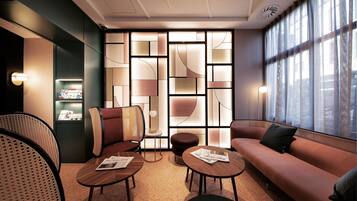Quarto de hotel moderno com sofá, duas mesas redondas, uma cadeira e um painel decorativo na parede.