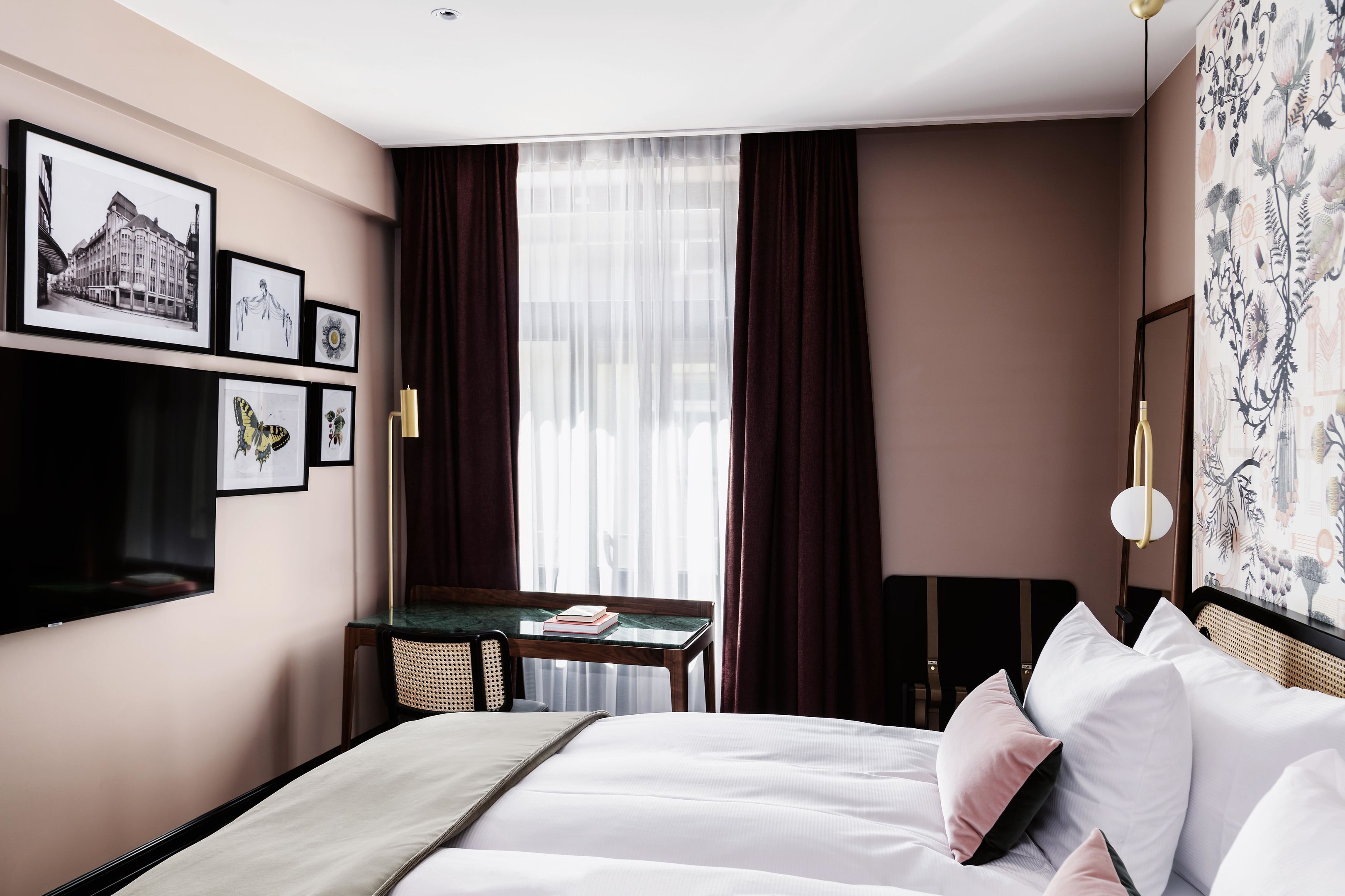 Quarto de hotel com cama, escrivaninha e uma grande janela com cortinas.