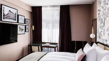 Quarto de hotel com cama, escrivaninha e uma grande janela com cortinas.