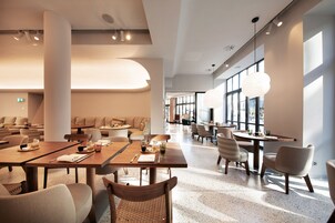 Um interior moderno com várias mesas e cadeiras para refeições, grandes janelas e um design limpo e minimalista.