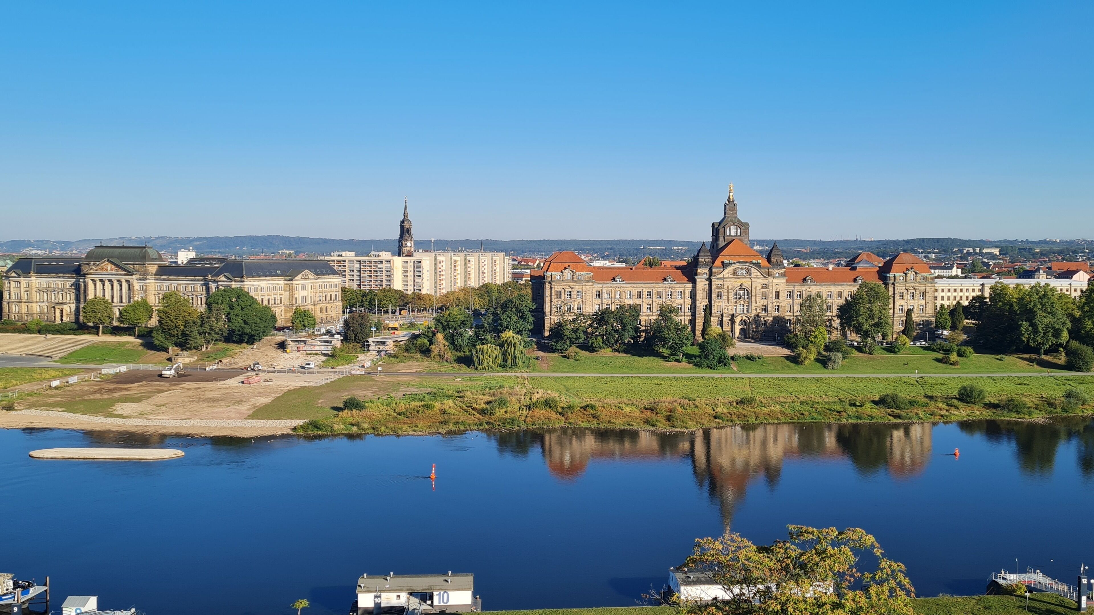 Um grande complexo de edifícios históricos com uma torre central, rodeado por um lago tranquilo e vegetação.