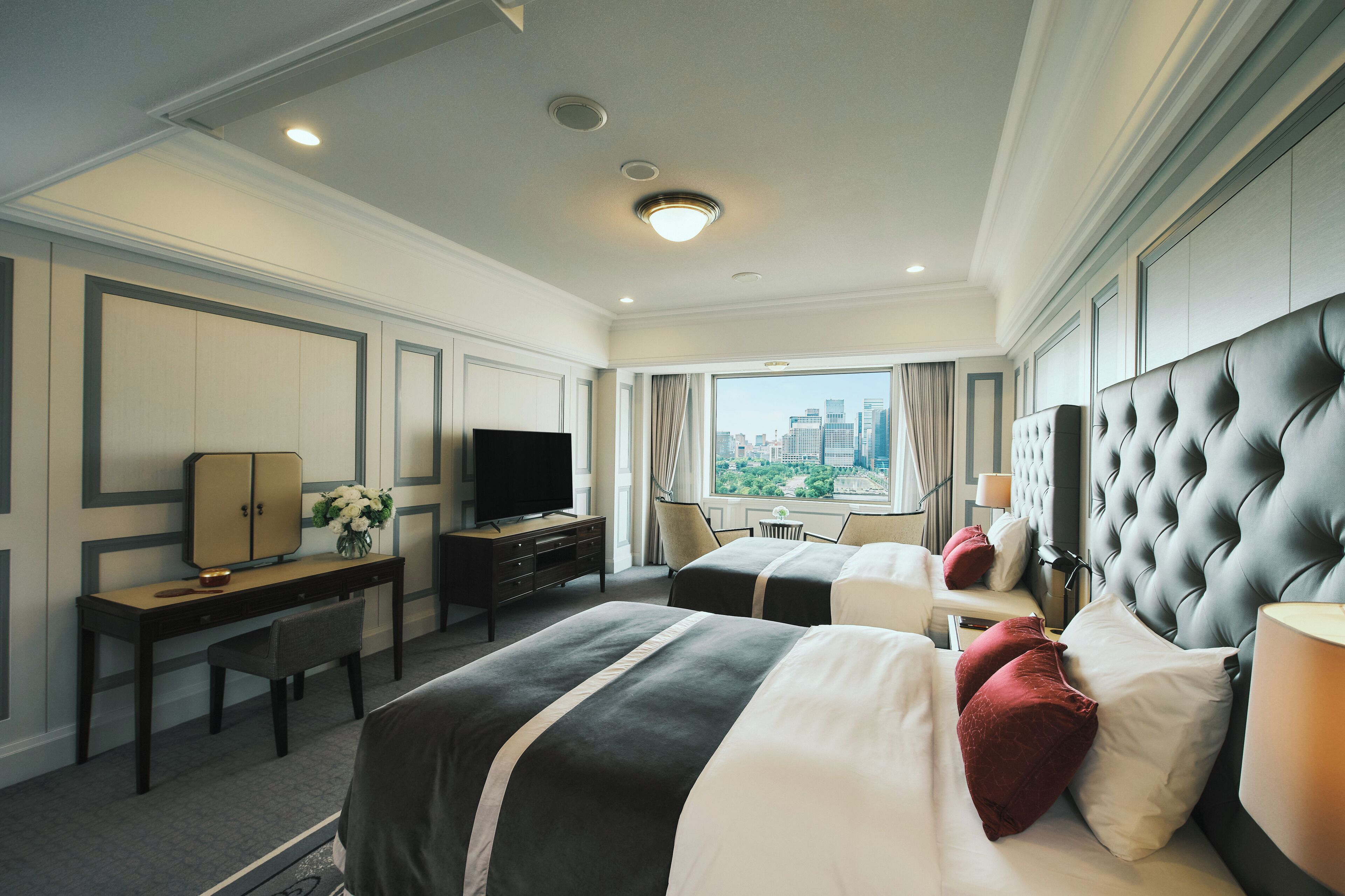 Quarto de hotel com duas camas, uma escrivaninha, televisão e vista para a cidade.