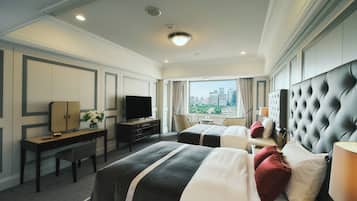 Quarto de hotel com duas camas, uma escrivaninha, televisão e vista para a cidade.