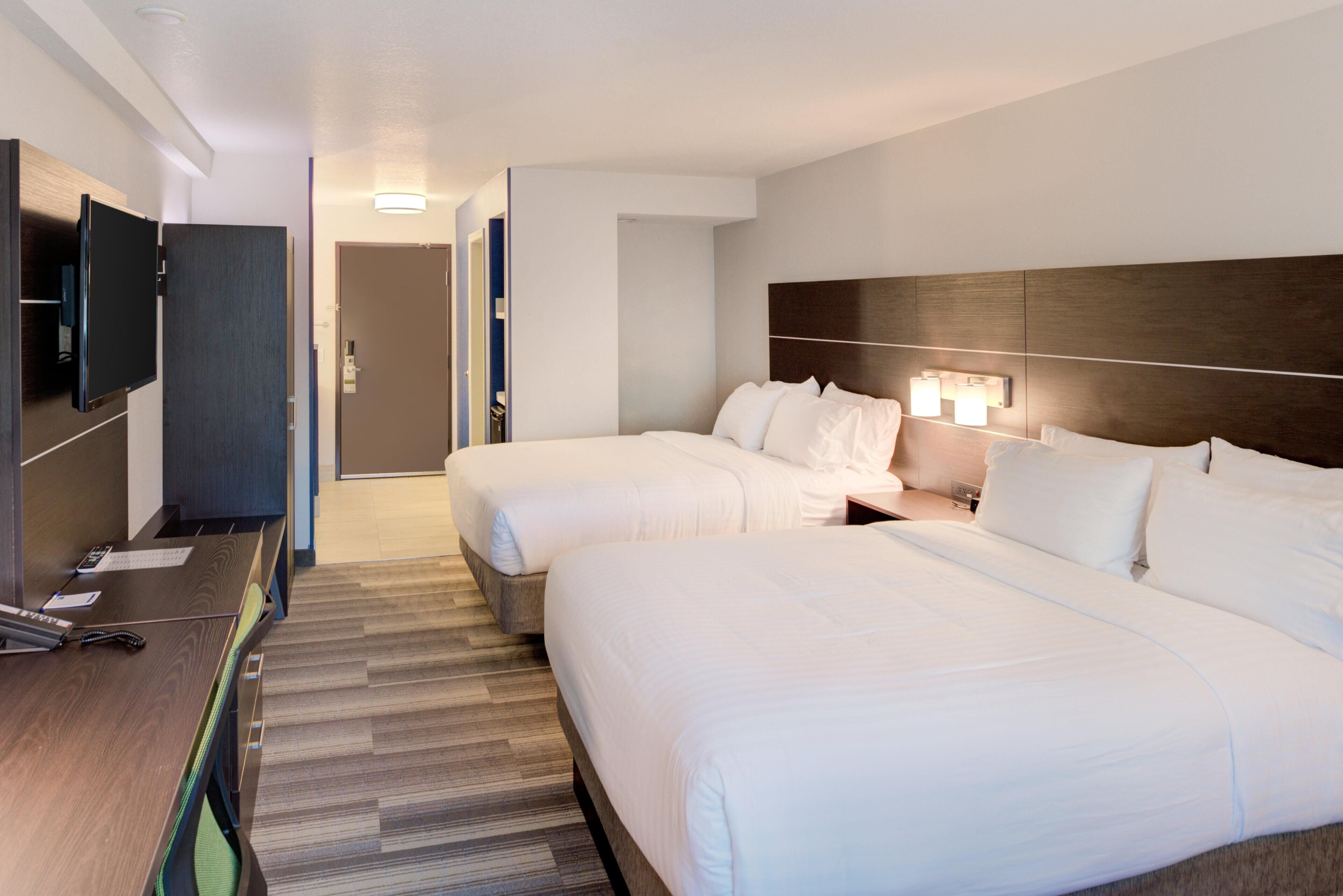 Quarto de hotel com duas camas, uma mesa, uma televisão e porta de acesso a um banheiro.