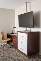 Quarto de hotel moderno com escrivaninha de madeira, uma cadeira, TV de tela plana na parede e carpete estampado.
