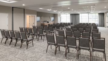 Uma sala de conferências com fileiras de cadeiras, um balcão de recepção e uma grande janela com cortinas.