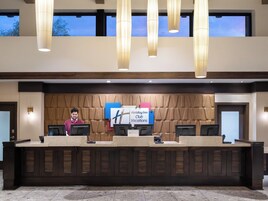 Uma receção de hotel com design moderno, apresentando um painel de parede de madeira e um ecrã grande exibindo o logótipo da Holiday Inn Club Vacations.