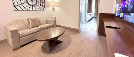 Uma sala de estar moderna com um sofá, uma mesa de centro, um abajur e uma TV fixada na parede.