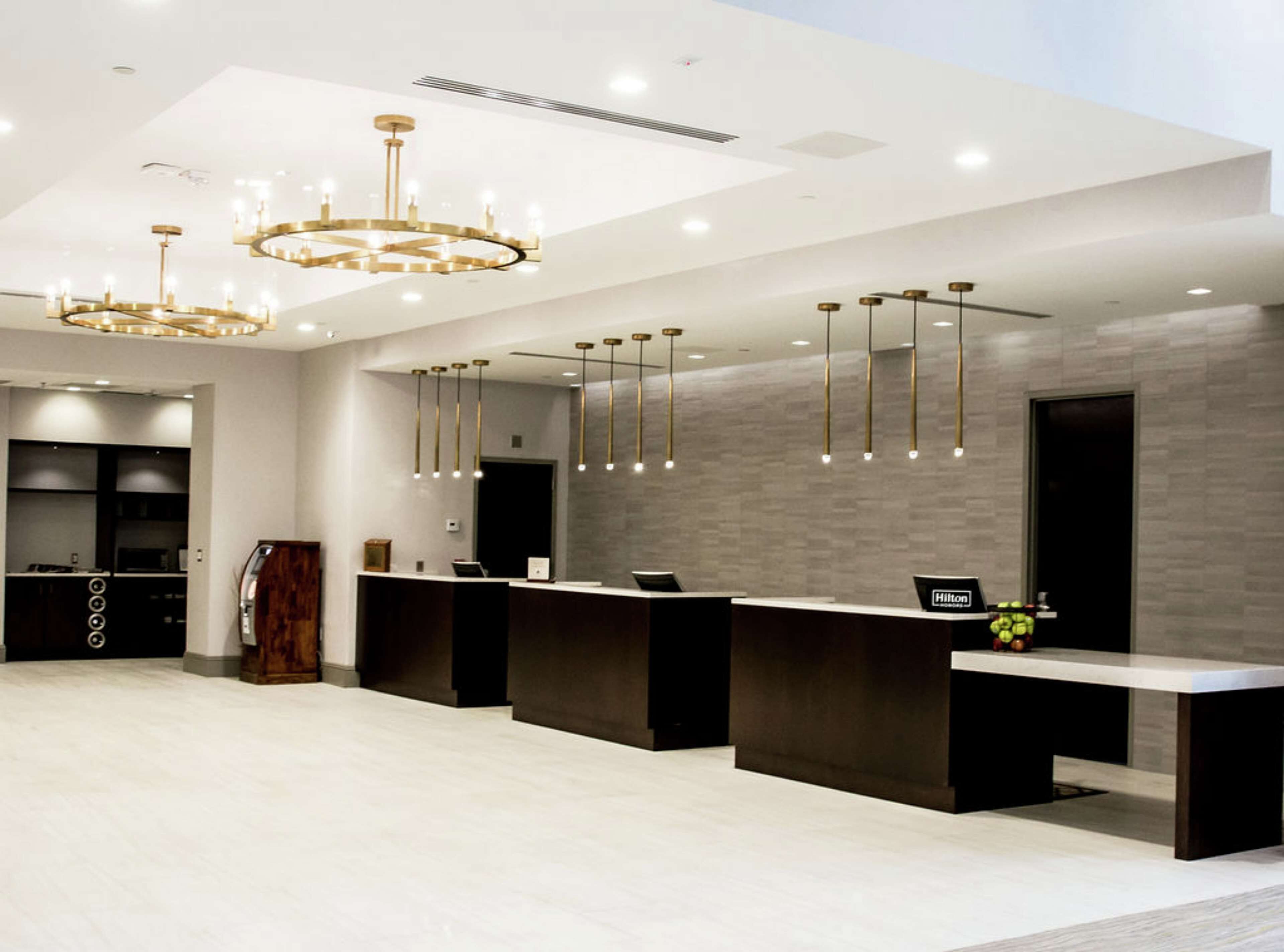 Uma área de recepção de hotel moderna, com um balcão central, vários postos de atendimento e um lustre.