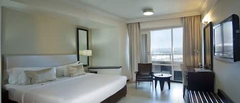 Quarto de hotel com uma cama grande, uma escrivaninha, uma cadeira e uma televisão.