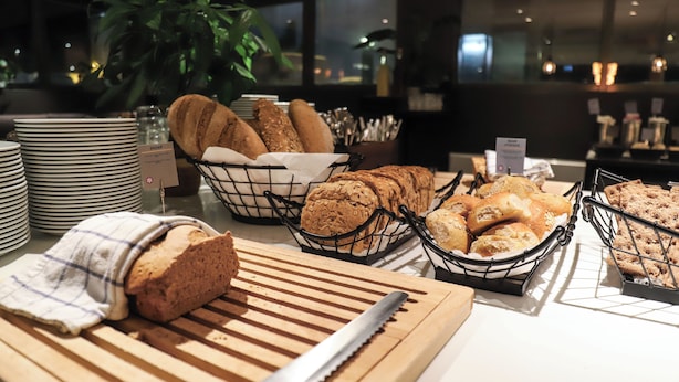 Um buffet com diversos pães e doces dispostos em cestas e numa tábua de corte.