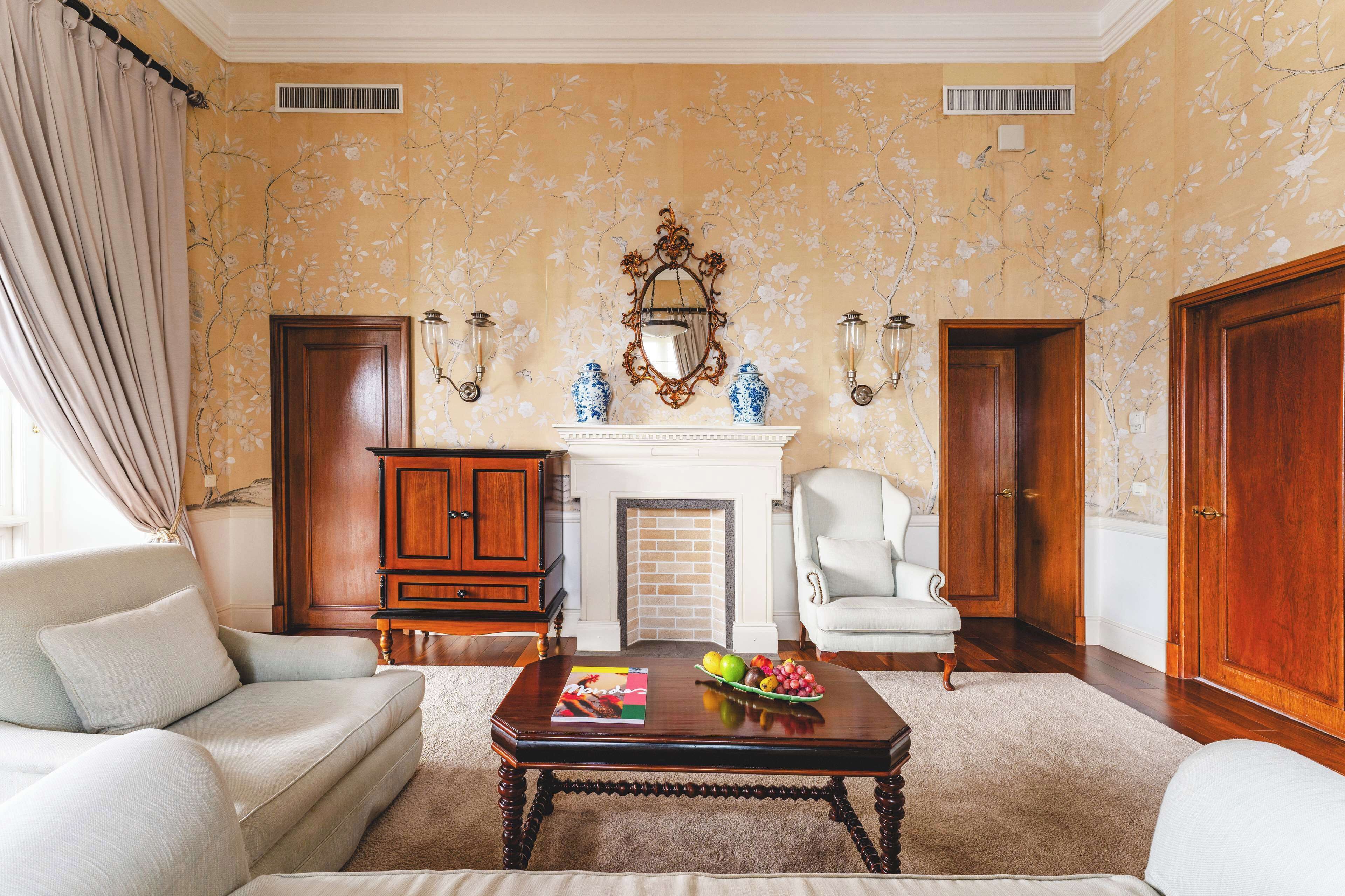 Sala de estar com lareira, sofá, mesa de centro com frutas e poltrona branca.