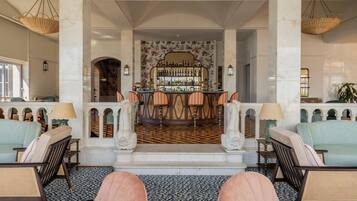 Uma área de bar com piso estampado, banquetas e balcão repleto de garrafas.