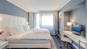 Quarto de hotel moderno com uma cama grande, uma escrivaninha com televisão de tela plana e uma cadeira.