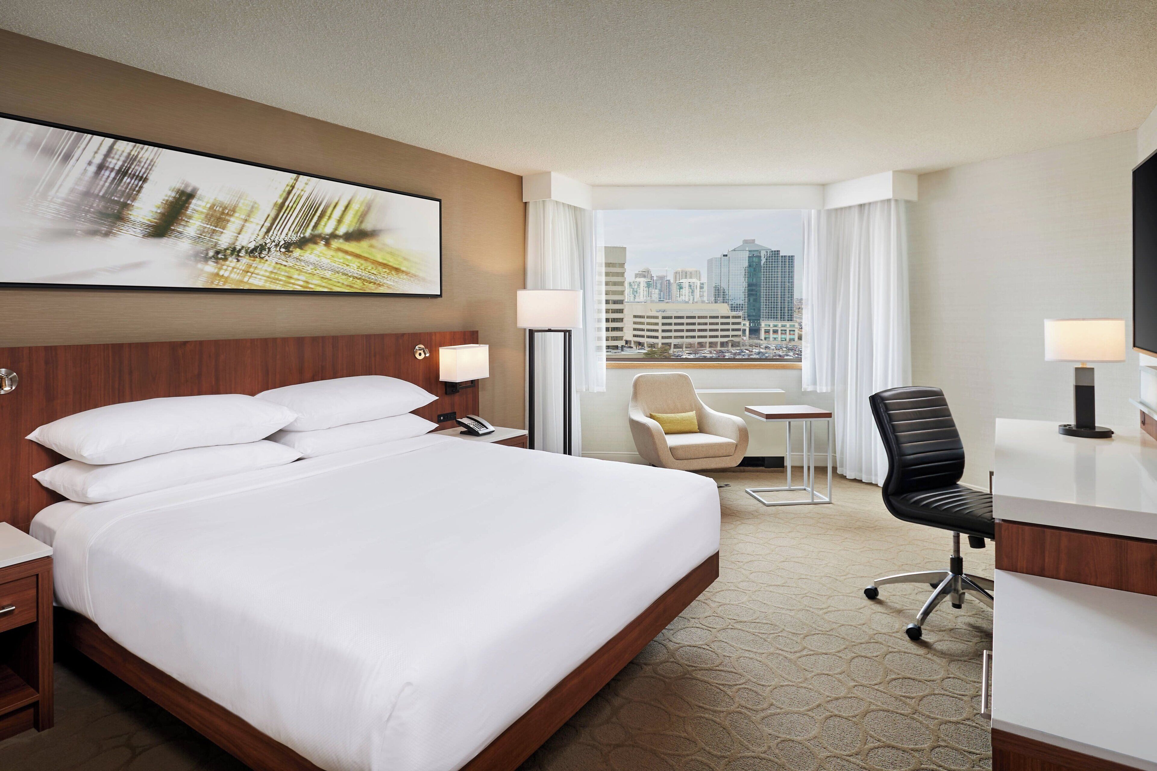 Quarto de hotel com uma cama grande, escrivaninha, cadeira e vista para a cidade.
