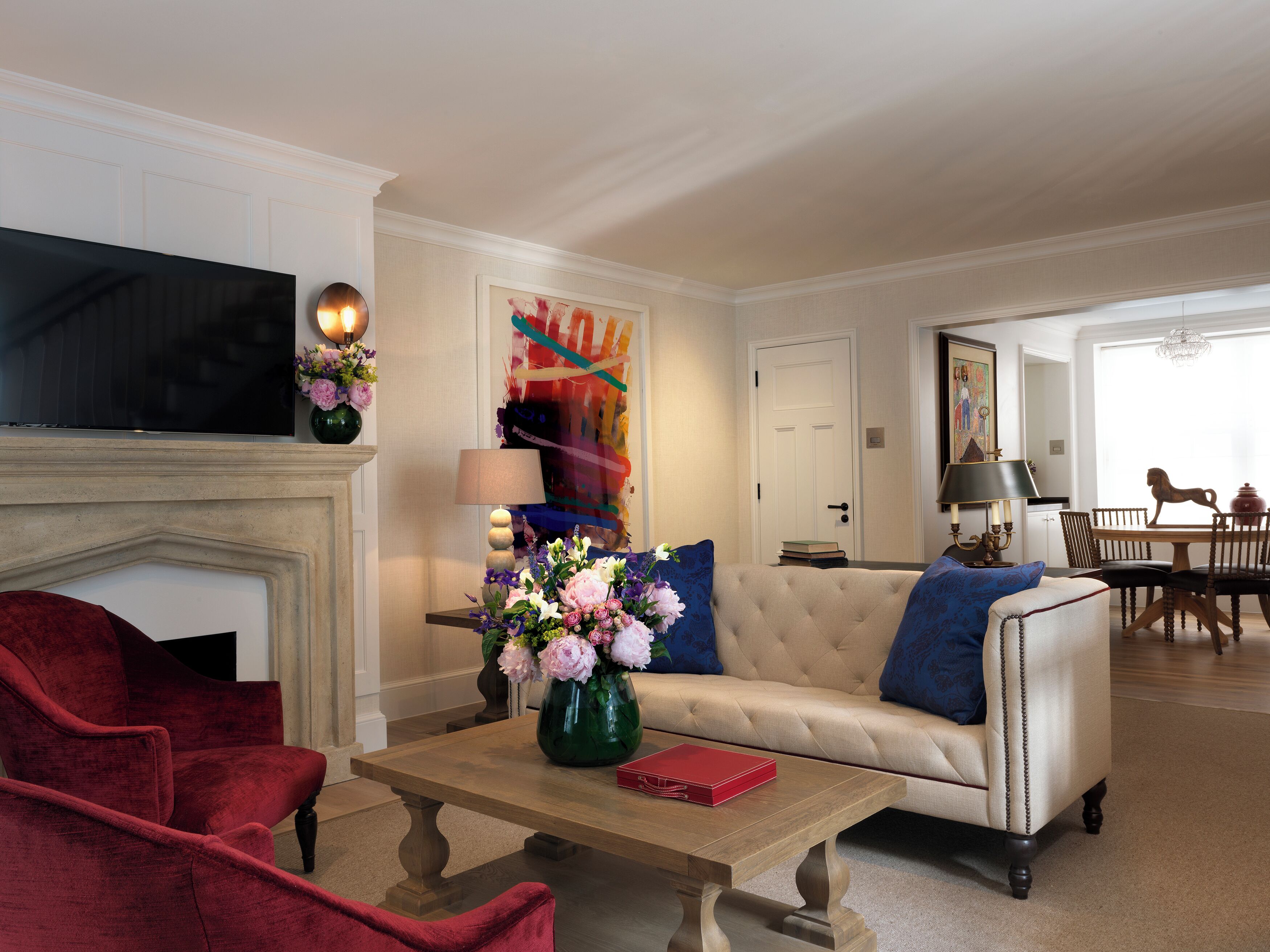 Uma sala de estar com lareira, um sofá, uma poltrona vermelha, uma mesa de centro e uma área de jantar com mesa e cadeiras.