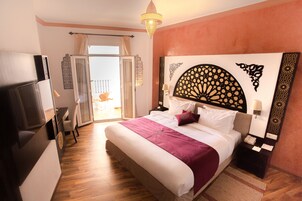 Quarto de hotel com uma cama grande, televisão, varanda e cabeceira decorativa.