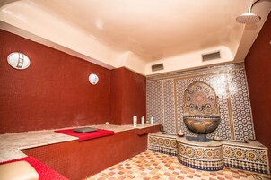 Casa de banho com parede vermelha, chão em azulejos, pia, espelho e chuveiro.