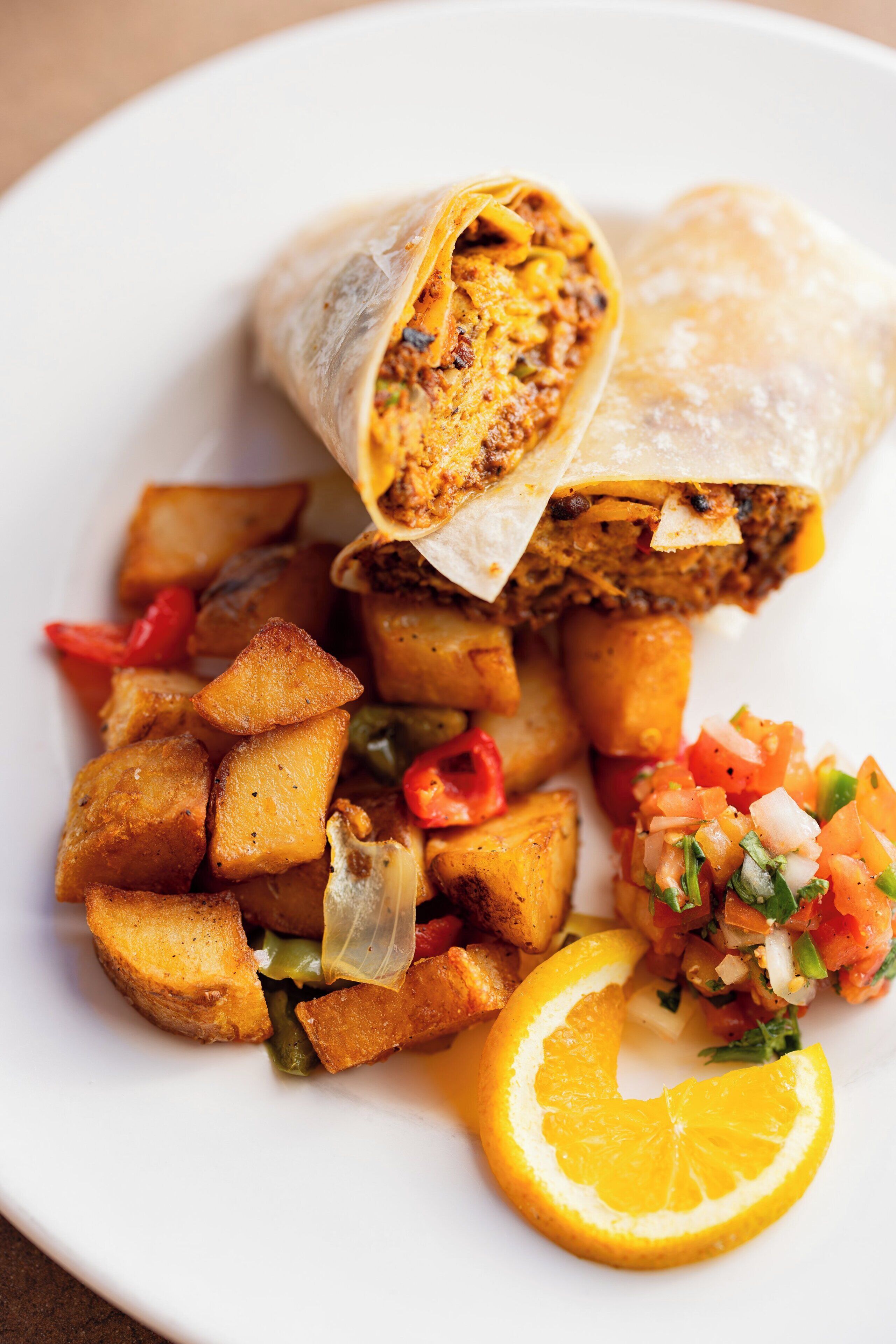 Um burrito acompanhado de batatas assadas, uma fatia de laranja e um pouco de salsa.
