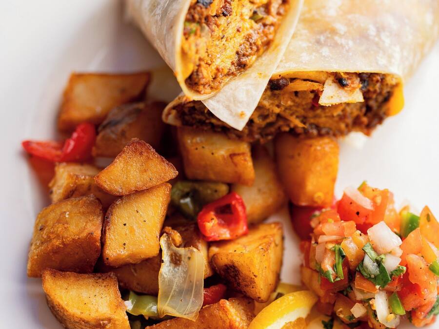 Um burrito acompanhado de batatas assadas, uma fatia de laranja e um pouco de salsa.