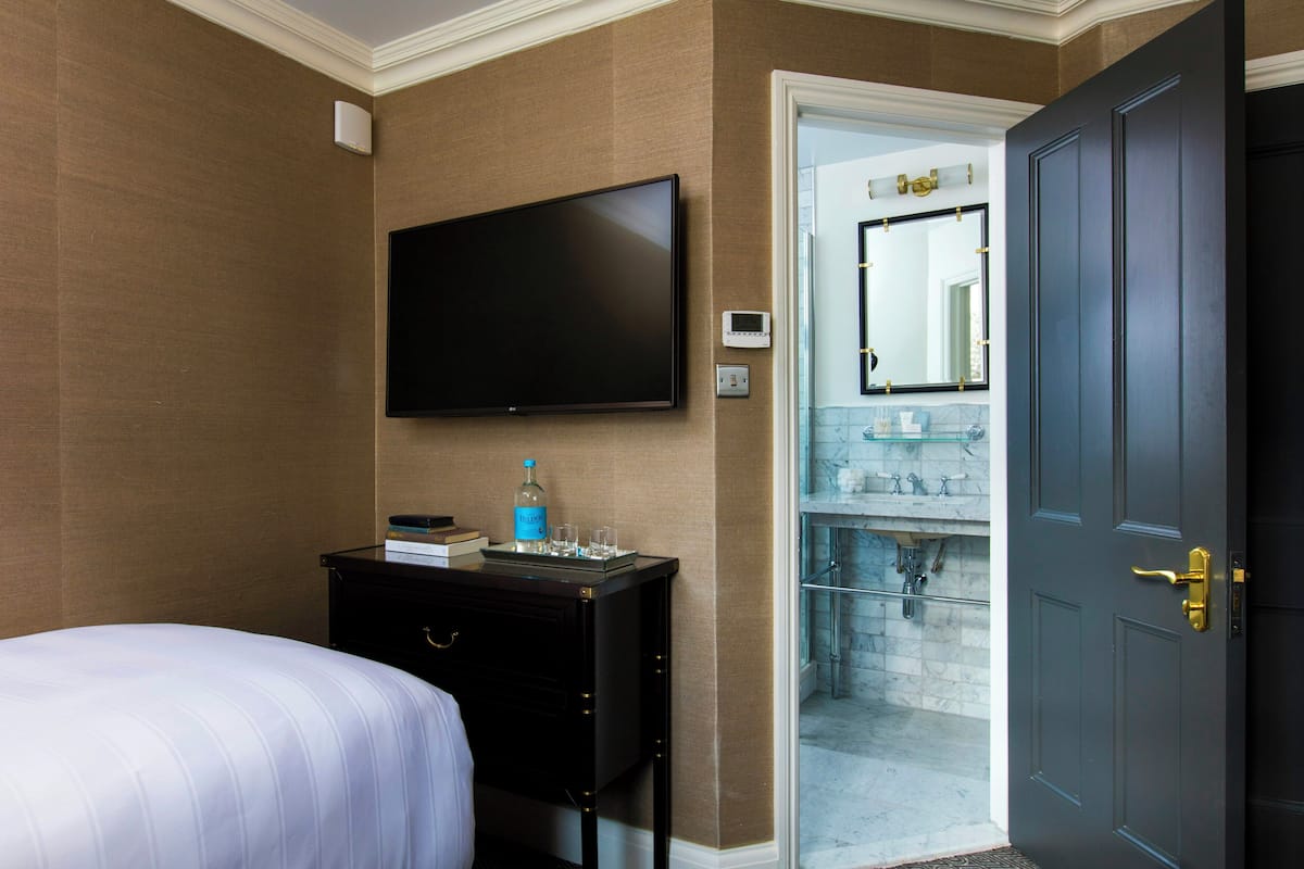 Quarto de hotel com uma cama, cômoda, televisão de tela plana, porta para banheiro com espelho e pia.