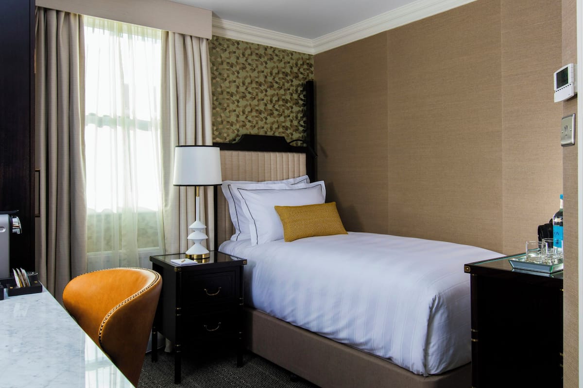 Quarto de hotel com cama, escrivaninha, cadeira, luminária e minibar.