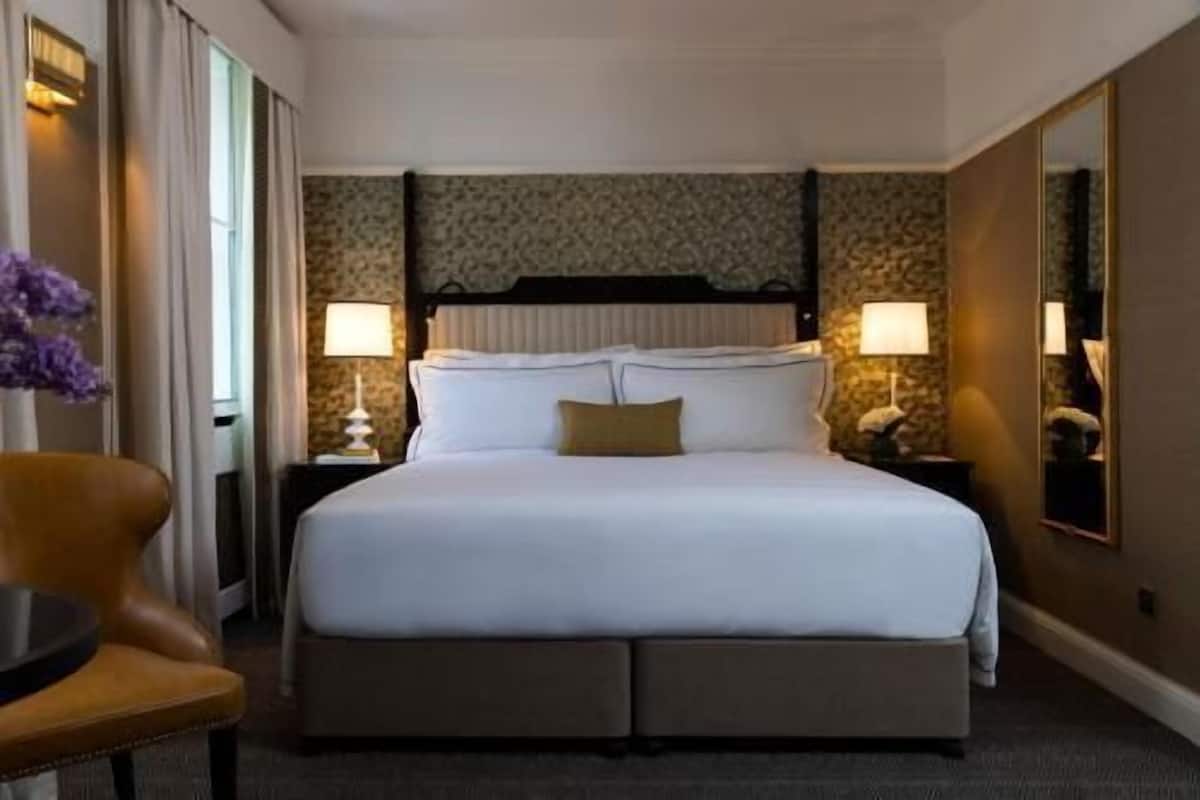 Quarto de hotel com uma cama grande, duas luminárias de cabeceira, uma cadeira e um espelho.
