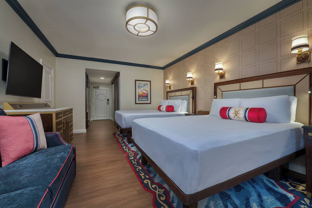 Quarto de hotel com duas camas, televisão, escrivaninha e corredor que dá para outro quarto.