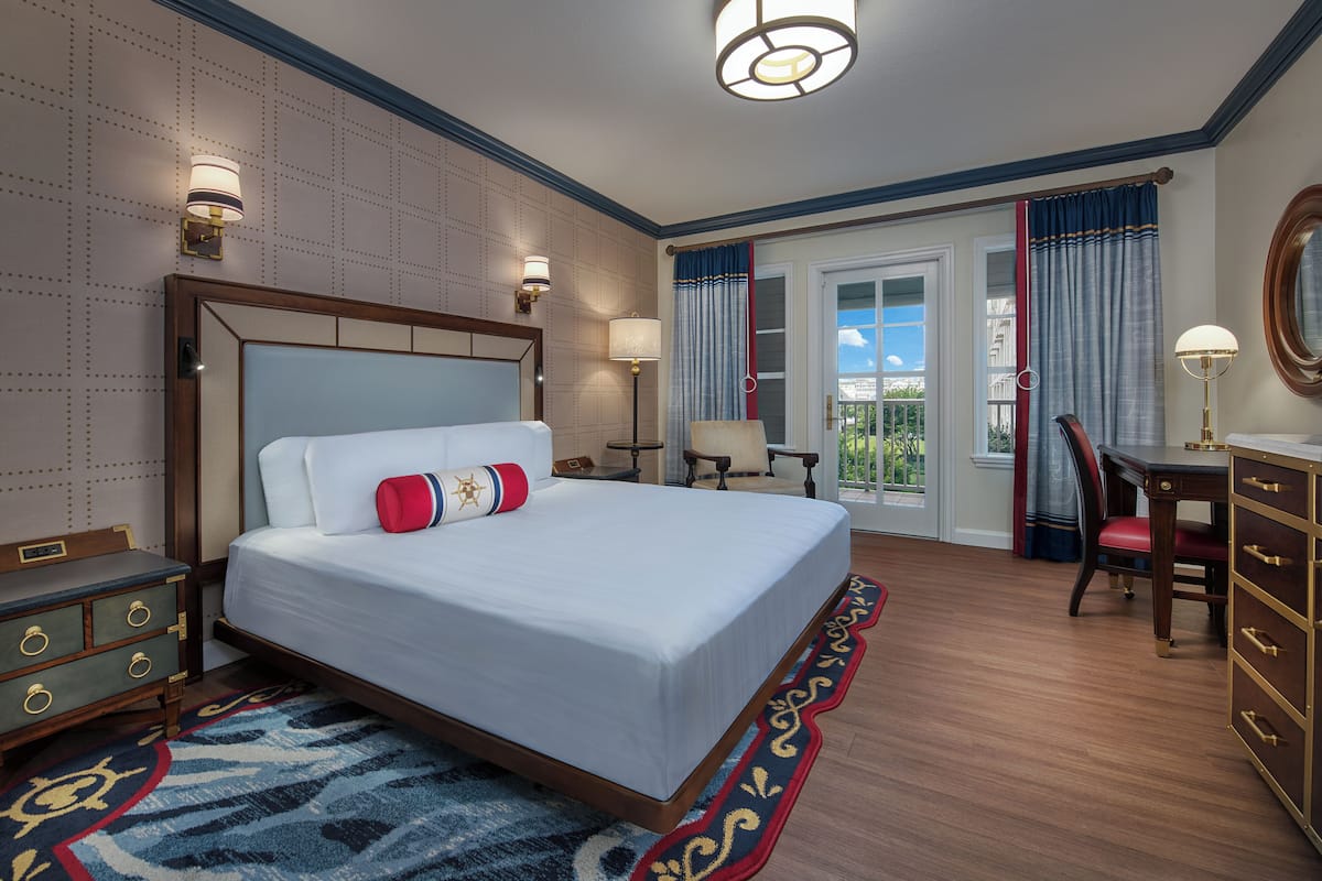 Quarto de hotel com uma cama grande, uma escrivaninha, uma cadeira e vista para o exterior.