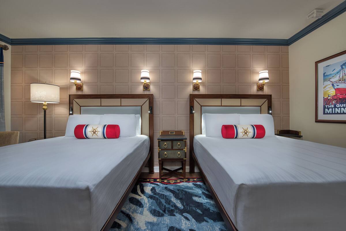 Quarto de hotel com duas camas, uma mesa de cabeceira e uma pequena mesa.