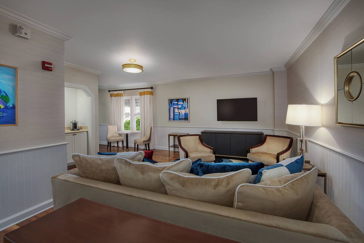 Sala de estar com sofá bege, mesa de centro de madeira, televisão de tela plana e área de jantar com mesa e cadeiras.