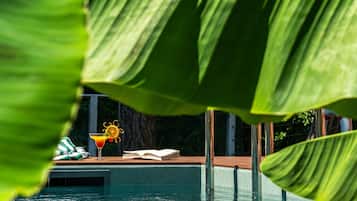 Uma área à beira da piscina com uma espreguiçadeira, uma bebida e um livro aberto.