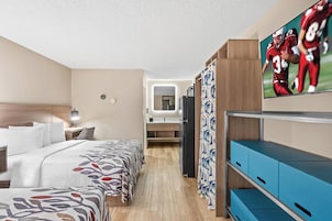 Quarto de hotel com cama, mesa de cabeceira, luminária, televisão, guarda-roupa e espelho.