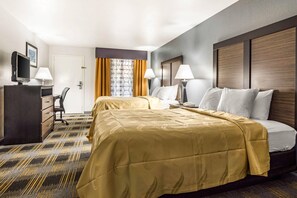 Quarto de hotel com duas camas, uma escrivaninha com computador e televisão.